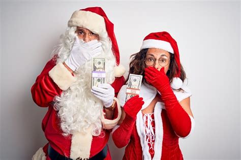 산타 클로스 의상을 입고 선임 부부는 실수로 손으로 입을 덮는 충격적인 고립 된 흰색 배경 위에 달러를 들고 비밀 개념입니다 2명에 대한 스톡 사진 및 기타 이미지 Istock