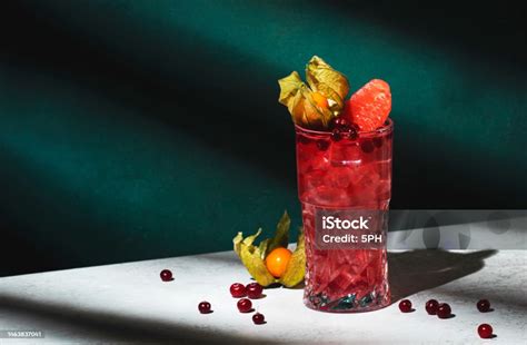보드카 크랜베리 자몽 주스 오렌지 및 얼음을 곁들인 바닷 바람 알코올 칵테일 Physalis로 장식 짙은 녹색 배경 단단한 빛과 그림자 패턴 칵테일에 대한 스톡 사진 및