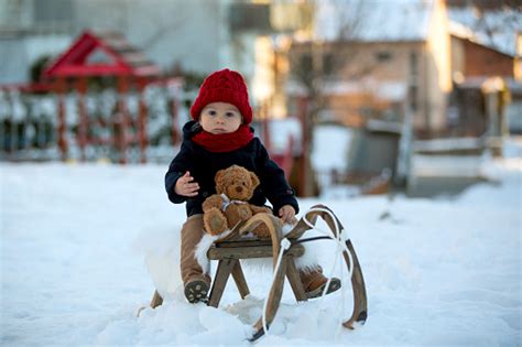 눈 겨울 시간에 테디와 놀고 아기 파란 코트를 입은 어린 소년 썰매를 타고 미끄러지며 테디 베어를 들고 겨울 공원에서 야외에서 놀기 겨울에 대한 스톡 사진 및 기타 이미지