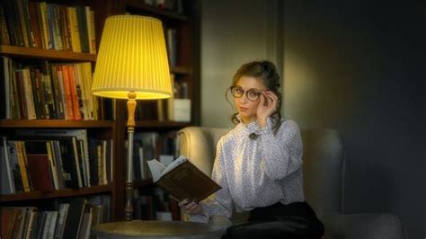 Обои на рабочий стол Девушка в очках в светлой блузке в горошек и в юбке сидит на кресле с