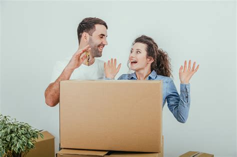 젊은 아내와 남편은 함께 큰 판지 상자 더미 뒤에 서 남자는 새 아파트의 열쇠를 들고 있다 여자는 감정적으로 반응 매우 행복하다 2명에 대한 스톡 사진 및 기타 이미지