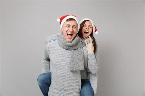 메리 재미 빨간색 산타 크리스마스 모자 회색 스웨터 스카프 회색 벽 배경 스튜디오 초상화에 고립 된 커플 여자 사람 행복 한 새 해 2019 축 하 휴일 파티 개념입니다