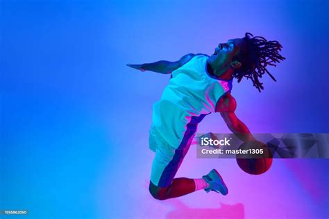 네온 불빛의 그라데이션 파란색 배경에 공을 들고 점프하는 프로 농구 선수의 역동적인 이미지 18 19세에 대한 스톡 사진 및