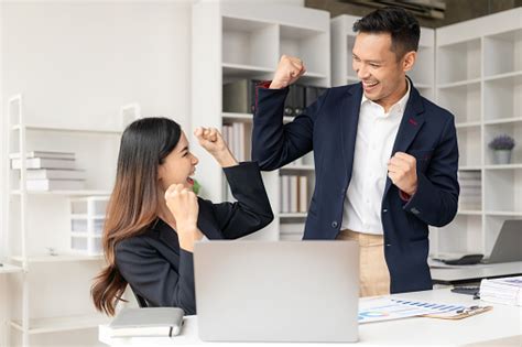 성공한 두 명의 젊은 아시아 사업가가 노트북 컴퓨터를 들고 기뻐하며 손을 들고 있다승리와 성공을 함께 축하하십시오 현대