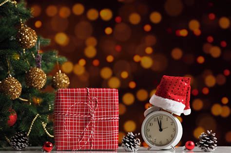 새해 구성 조명의 흐릿한 배경에 장식 된 크리스마스 트리 옆에 산타 모자에 선물 상자와 알람 시계 0명에 대한 스톡 사진 및 기타 이미지 Istock