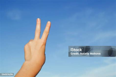 푸른 하늘의 배경에 대한 손은 승리 또는 평화의 표시를 보여 주며 라틴어 문자 V의 형태로 위쪽을 가리키는 손의 인덱스와 가운데 손가락으로 표시됩니다 개념에 대한 스톡 사진