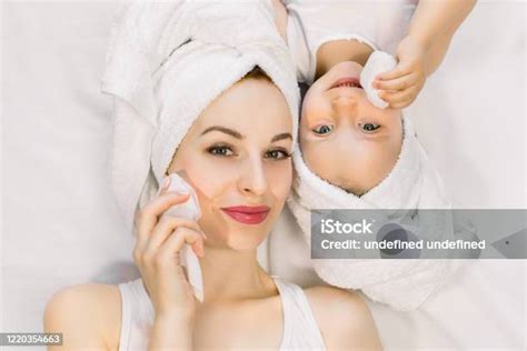매력적인 젊은 백인 어머니와 목욕 후 그녀의 작은 귀여운 딸의 초상화 머리에 흰색 목욕 수건을 입고 나쁜에 누워 젖은 물티슈로 얼굴을 청소 맨 위 보기 어머니에 대한 스톡