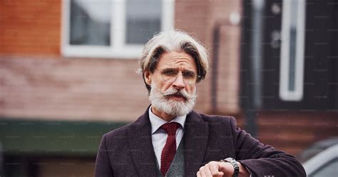 회색 머리와 수염을 가진 세련된 노인은 그의 시계에 그의 차 Cheks 시간 근처 거리에서 야외에 있습니다 사진 Unsplash의 양복 이미지