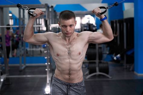 Мускулистый чувак с голым торсом тренируется в тренажерном зале делая