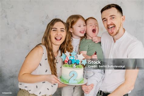 엄마 아빠 딸은 스튜디오의 회색 벽 근처에서 아들의 생일을 축하합니다 행복한 가족은 케이크를 들고 생일 파티를 축하하는 즐거운 시간을 보내고 있습니다 어머니 아버지는