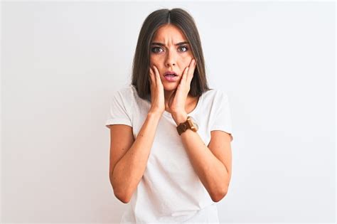 고립 된 흰색 배경 위에 서있는 캐주얼 한 티셔츠를 입은 젊은 아름다운 여성은 얼굴에 손을 들고 두려워하고 놀랍고 놀란 표정을 짓고 있습니다 T 셔츠에 대한 스톡 사진 및