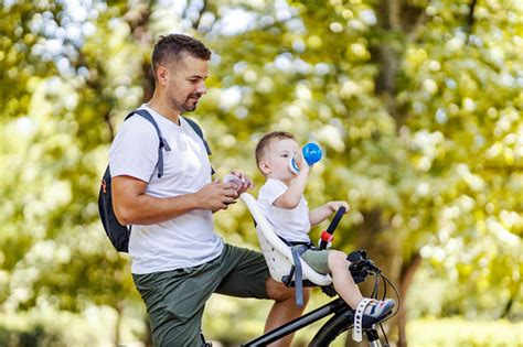 긴 자전거를 타고 잠시 멈춥다 활동적인 가족 활동 중에 상쾌한 추위를 마신 유아 한 소년이 자전거 바구니에 앉아 파란색 병에서 물을 마시고 성인 남성이 그 뒤에 앉아 있는
