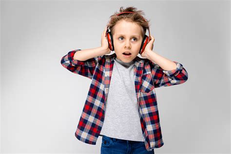 잘생긴 소년 격자 무늬 셔츠 회색 셔츠와 청바지에 회색 배경에 서 있다 빨간 헤드폰에서 소년입니다 소년은 그의 헤드폰을 들고 있다 개념에 대한 스톡 사진 및 기타 이미지