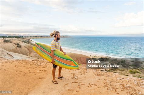 아름다운 금발의 호주 힙스터 서퍼는 해질녘에 시원한 빈티지 서핑 보드를 들고 바다를 바라보는 공포와 수염을 가지고 있습니다 다시 서핑으로 야외 는 뉴 노멀에서 스포츠