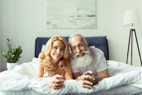 Happy Mature Couple In Love Lying Together In Bed And Smiling At Camera