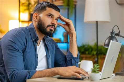 Bored Sleepy Young Indian Man Working On Laptop Computer Leaning On Hand At Home Office Stock