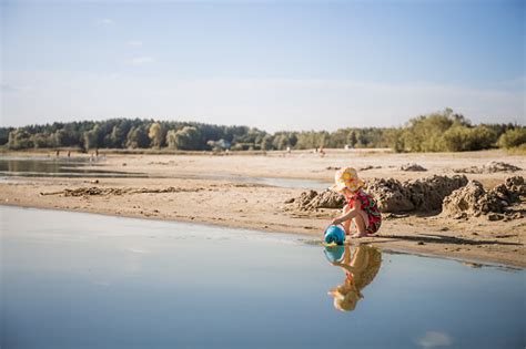 빨간 드레스를 입은 한 어린 2세 소녀가 손에 양동이와 머리에 파나마 모자를 쓰고 모래 사장을 따라 걷고 있습니다 더운 화창한 여름 날 자연 풍경 배경 공간을 복사합니다