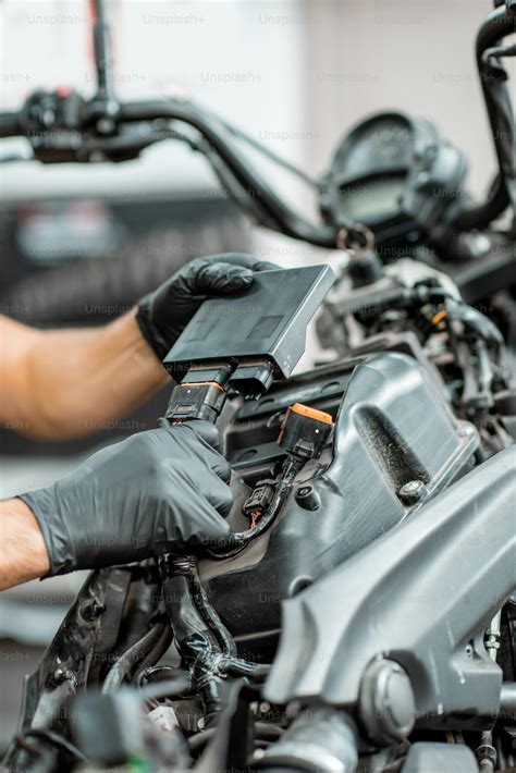 작업장에서 수리하는 동안 오토바이의 배선을 연결하는 보호 장갑을 낀 전기 기사 또는 수리공 클로즈업 사진 Unsplash의