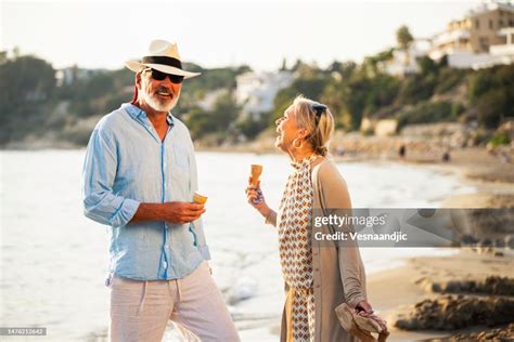 Happy Mature Couple On Vacation Walking By The Sea Eating Ice Cream