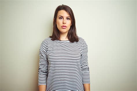 젊은 아름 다운 갈색 머리 여자 얼굴에 심각한 표정흰색 고립 된 배경 에 줄무늬 스웨터를 입고 카메라를 보는 간단하고 자연스러운
