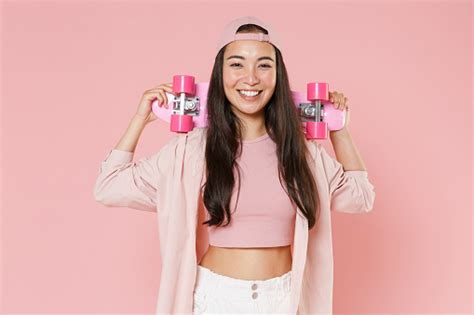 캐주얼 한 옷을 입고 미소 짓는 젊은 아시아 여성 소녀 파스텔 핑크 벽 배경 스튜디오 초상화에 고립 된 포즈를 취하는 모자 사람들은 진지한 감정 라이프 스타일 개념 복사