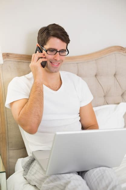 Premium Photo Casual Smiling Man Using Cellphone And Laptop In Bed