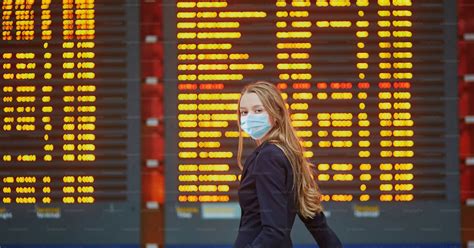 국제 공항 터미널에서 수하물과 함께 보호용 안면 마스크를 착용하고 정보 보드를 보고 항공편을 확인하는 여성 여행 가방을 든 객실 승무원 팬데믹 기간 동안의 여행 사진