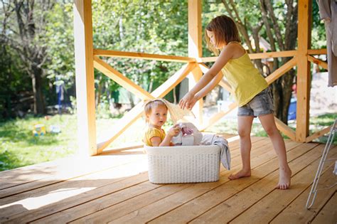 소녀 자매는 집안일을 돕고 아이들은 세탁을 위해 바닥 건조기에 플라스틱 바구니에서 씻은 세탁물을 걸어 놓고 집 근처 뒤뜰에서 여름에는 2 3 살에 대한 스톡 사진 및 기타