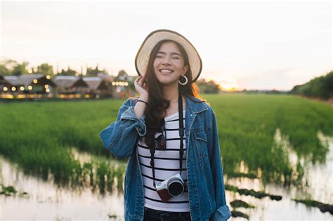 젊은 아시아 여자 모자에 카메라와 함께 웃 고 석양과 아름 다운 자연에서 즐기는 소녀 여행 여름 휴가 휴가 휴식 개념 관광객에