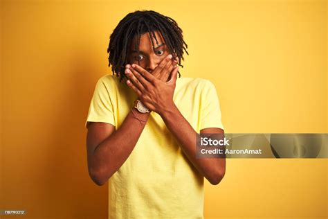 고립 된 노란색 배경 위에 서있는 캐주얼 한 티셔츠를 입은 공포를 가진 아프로 남자는 실수로 손으로 입을 덮는 충격을 받았습니다 비밀 개념입니다 T 셔츠에 대한 스톡 사진