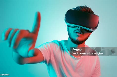 매력적인 수염된 남자 Vr 헤드셋과 Poniting를 시도 하 고입니다 가상 현실과 또 다른 세계를 탐험 하는 젊은 남자는 화려한 배경에 고글 기술자에 대한 스톡 사진 및