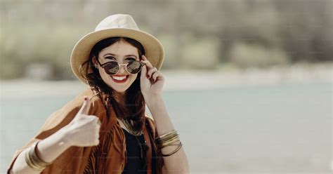 세련된 여행자 힙스터 여성은 모자 가죽 가방 프린지 판초 및 액세서리가 있는 선글라스를 끼고 엄지손가락을 치켜들고 웃고 있습니다 행복한 보헤미안 소녀 룩 방랑벽 여름