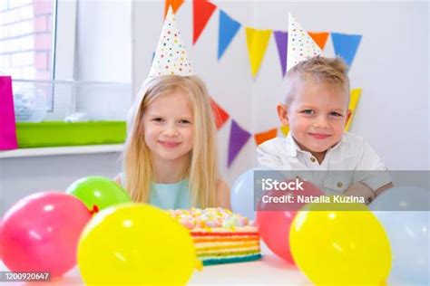 두 금발 백인 아이 소년과 생일 모자에 여자 카메라를보고 생일 파티에서 미소 풍선과 생일 무지개 케이크 다채로운 배경 가족에 대한 스톡 사진 및 기타 이미지 Istock