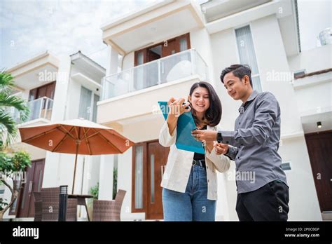 Asian Female Real Estate Agent Showing Clipboard Chatting With Man