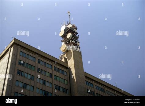 Communication Tower With Multiple Antennas On Top Of A Concrete Building Against A Clear Blue
