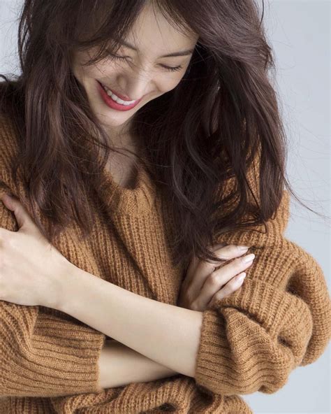 A Woman With Her Arms Crossed Looking Down At The Ground And Smiling
