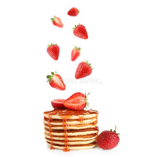 fresh strawberries falling onto stacked pancakes against white