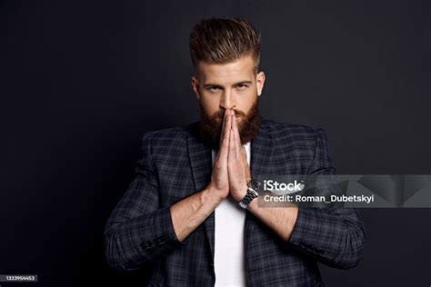 뭔가에 대해 생각 완벽한 헤어스타일과 수염을 가진 자신감 있는 남자가 그의 얼굴에 손을 잡고 기도하며 회색 배경에 서 있습니다