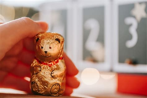 과자가 있는 강림절 달력 밝고 아늑한 방에서 크리스마스 트리 배경에 어린이 손에 강림절 달력과 함께 금박 호일 행의 초콜릿 곰 크리스마스 전통 새해를 위한 선물과 놀라움