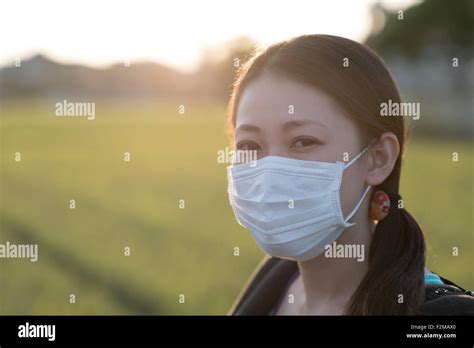 A Young Japanese Woman Wearing A Surgical Mask Outdoors In The Countryside With A Bright Sunset