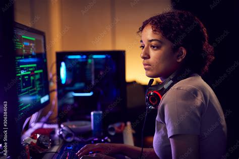 Female Teenage Hacker Sitting In Front Of Computer Screens Bypassing Cyber Security Stock Photo