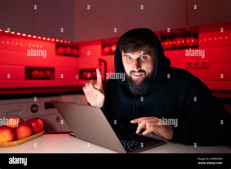A Male Hacker Behind A Laptop In A Dark Room Points His Finger Up Stock