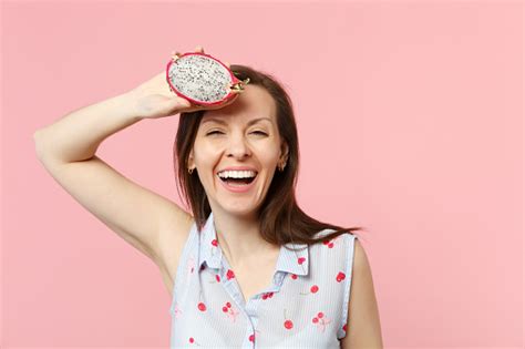 스튜디오에서 분홍색 파스텔 배경에 고립 된 신선한 잘 익은 피타 야 용 과일의 절반을 들고 여름 옷에 젊은 여자를 웃 고 사람들은 생생한 라이프 스타일 휴식 휴가 개념입니다