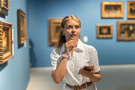 молодая девушка с информационным буклетом смотрит на картины на художественной выставке в музее