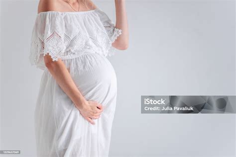 흰색 모자를 쓴 아기를 기대하며 한 젊은 임산부가 배를 껴안고 있다 미니멀하고 고립 된 배경 복사 공간에서 부드러운 소녀 행복한 출산 임신 대리 드레스에 대한 스톡 사진 및