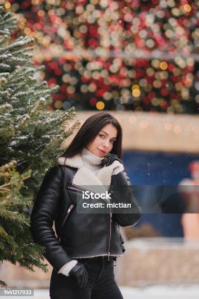 따뜻하고 아늑한 옷을 입은 아름다운 백인 여성이 축제 조명을 배경으로 눈이 내리면서 크리스마스 박람회에서 야외로 걸어갑니다 12월 31일에 대한 스톡 사진 및 기타 이미지