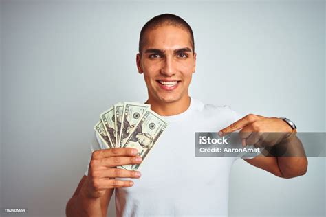 젊은 잘 생긴 남자 들고 달러 위에 흰색 고립 된 배경 와 깜짝 얼굴 가리키는 손가락 에 자신 가리키기에 대한 스톡 사진 및 기타 이미지 Istock