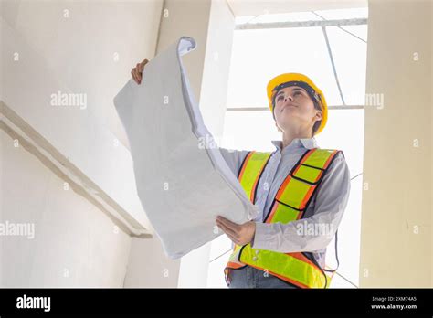 Confident Female Architect In Safety Gear Holding Blueprints And Inspecting Construction Site