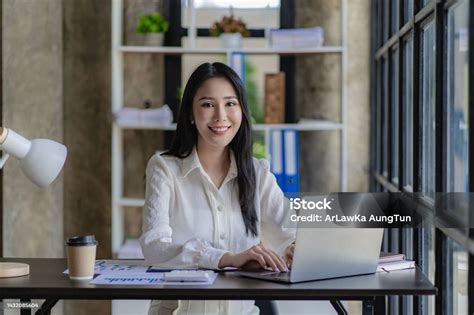 책상에 계산기와 비즈니스 보고서가있는 창 근처의 현대 사무실에서 재무 그래프 문서가있는 랩톱 컴퓨터에서 일하는 아시아 사업가 재정 고문에 대한 스톡 사진 및 기타 이미지