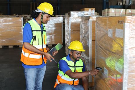 안전모와 반사 재킷을 입은 창고 노동자 그룹이 소매 창고 물류 유통 센터의 생산 재고 및 재고로 배달하기 위해 대형 상자 패키지의 바코드를 스캔합니다 20 24세에 대한